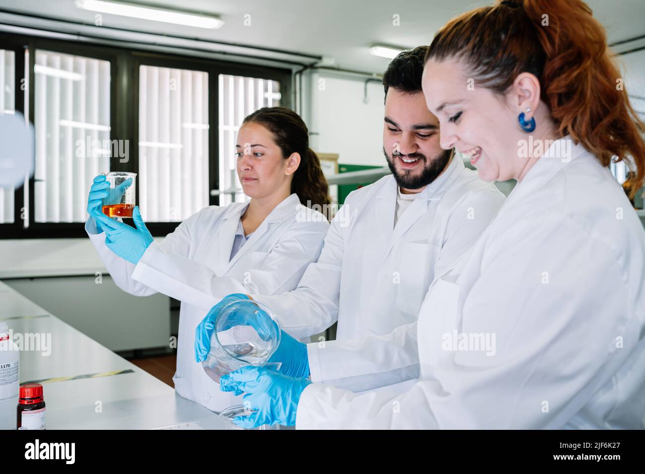 Group of positive colleagues in white uniforms preparing chemical ...