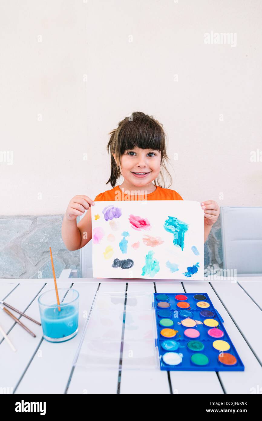 Positive girl looking at camera and demonstrating paper with colorful ...