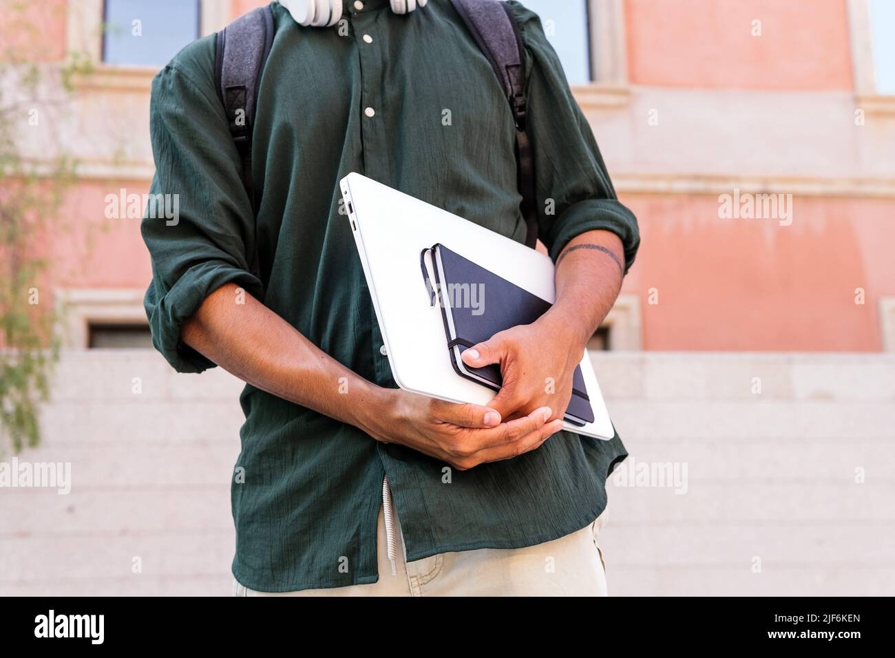 Low angle of anonymous male student with netbook and headphones while ...