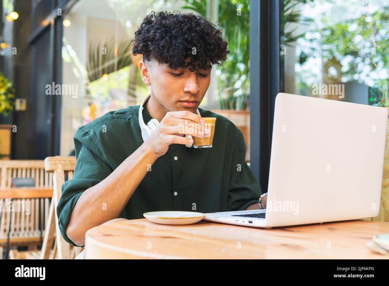 Ethnic male freelancer with curly hair drinking coffee while working ...