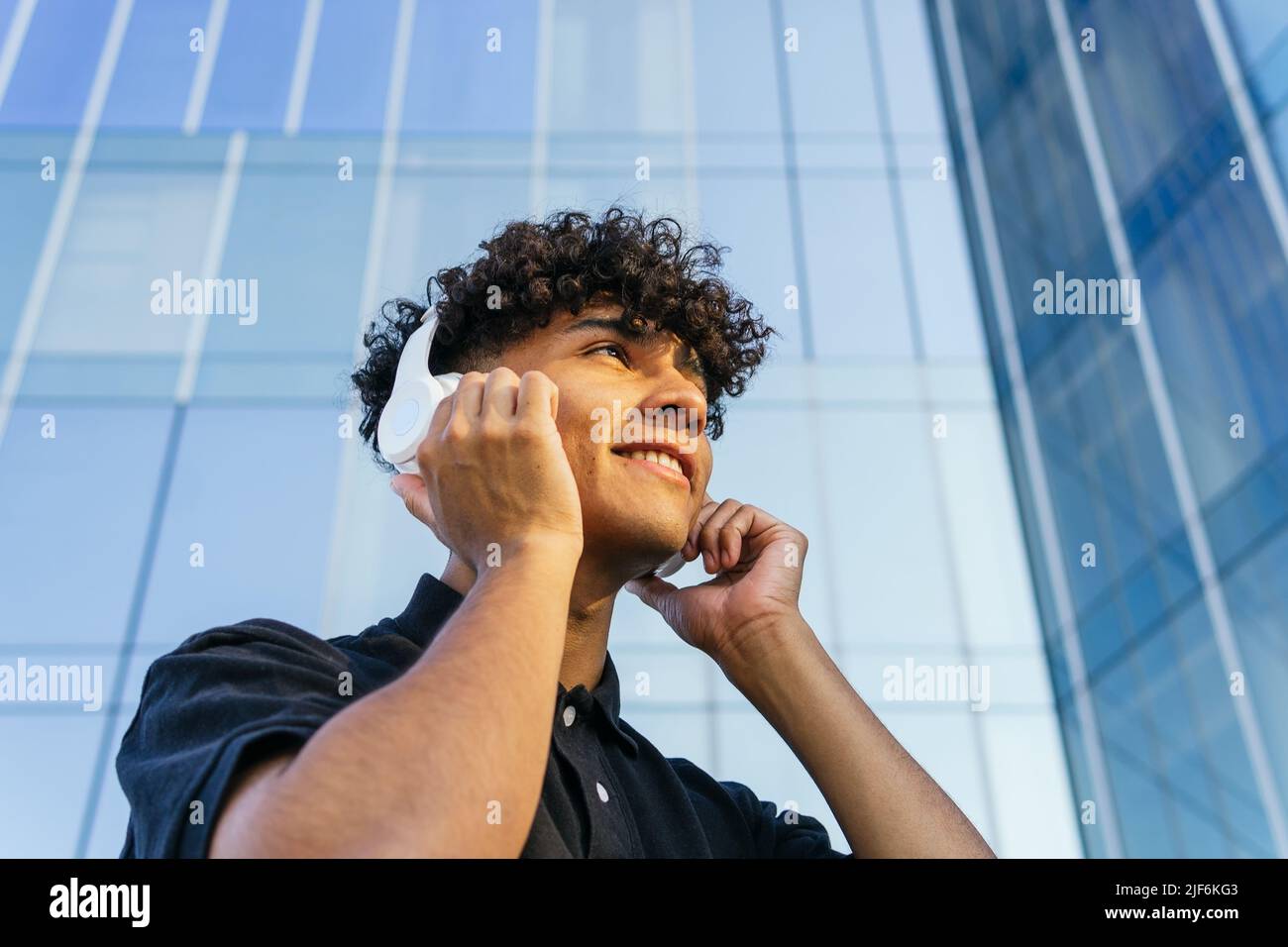 Low angle of young male in modern headphones listening music while ...