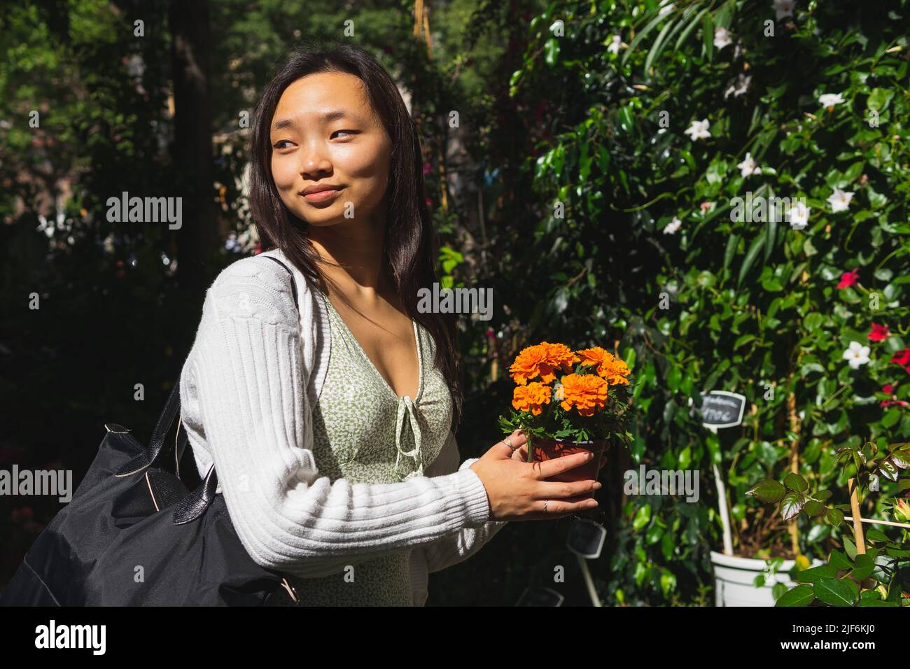 Side view of glad Asian female choosing colorful potted flowers while ...