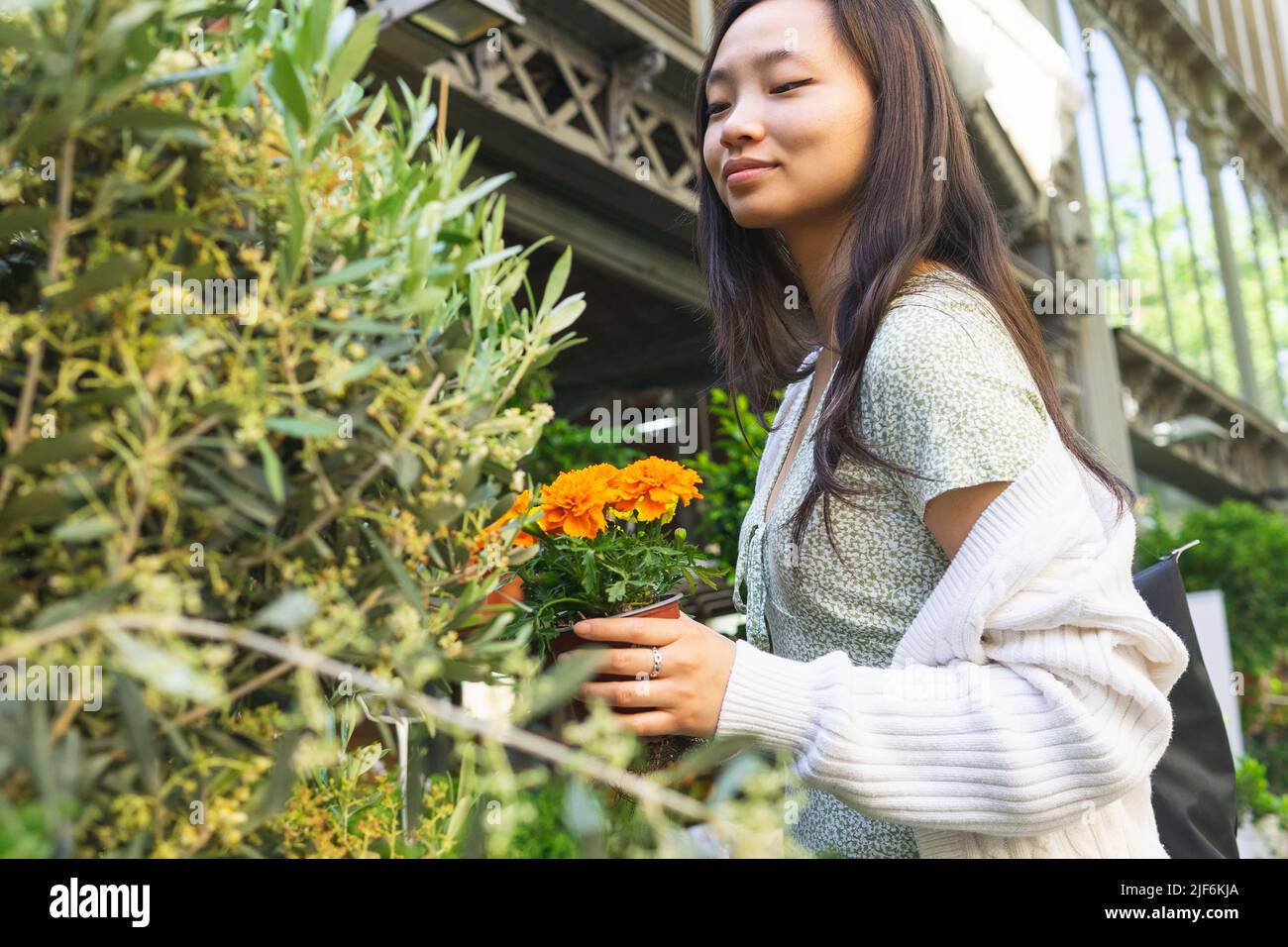 Side view of glad Asian female choosing colorful potted flowers while ...
