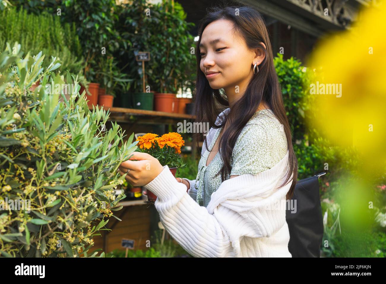 Side view of glad Asian female choosing colorful potted flowers while ...