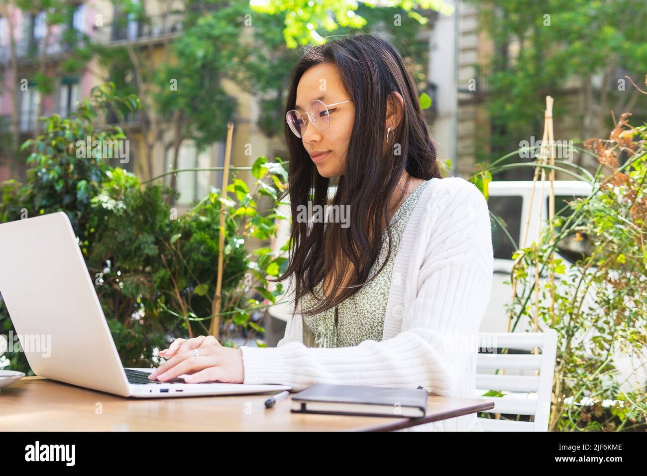 Serious focused Asian female freelancer while sitting at table with ...