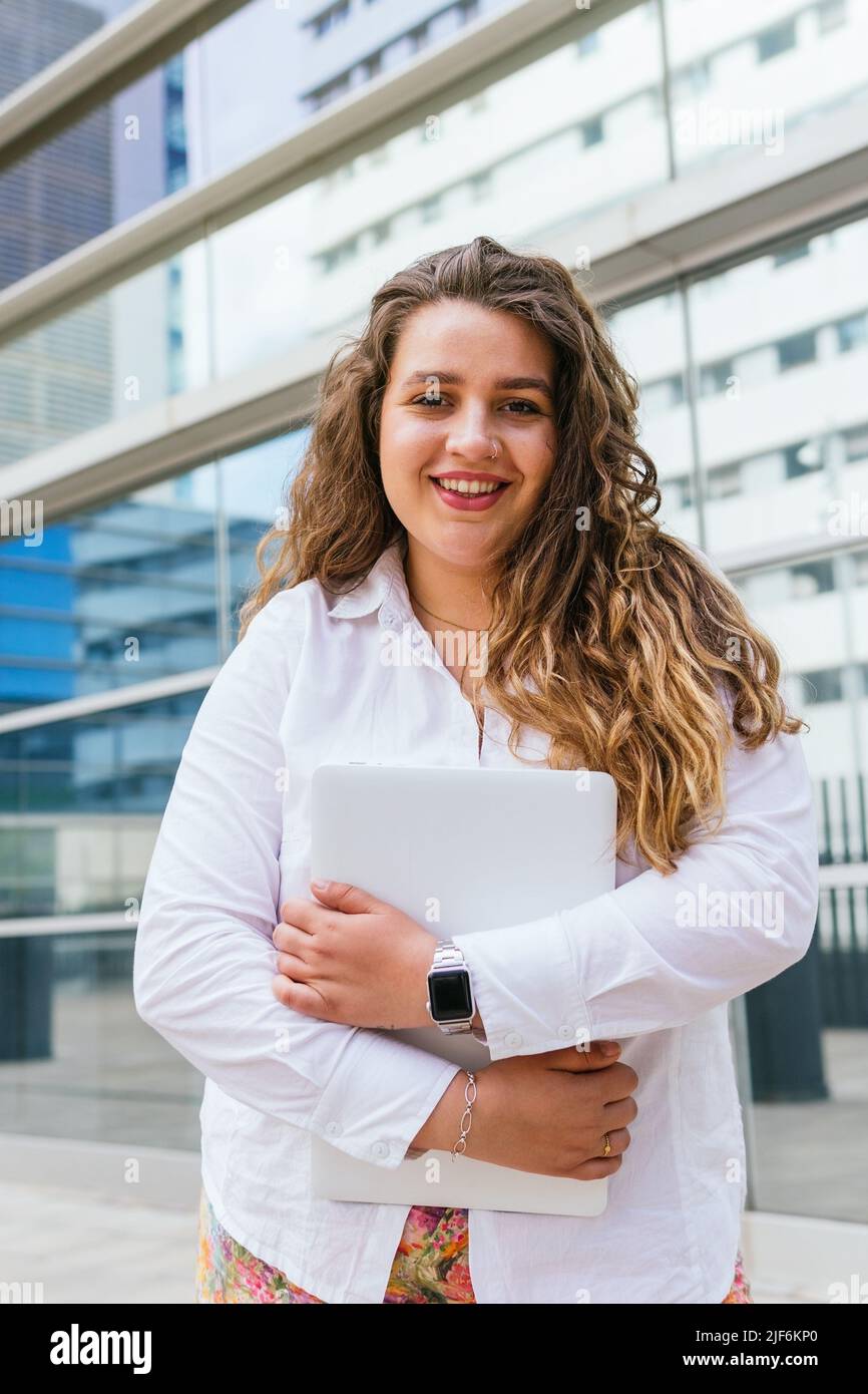 Optimistic female with netbook looking at camera standing near modern ...