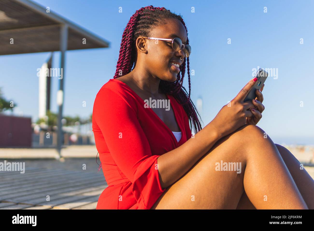 African American young Woman in trendy red dress and braids using phone ...