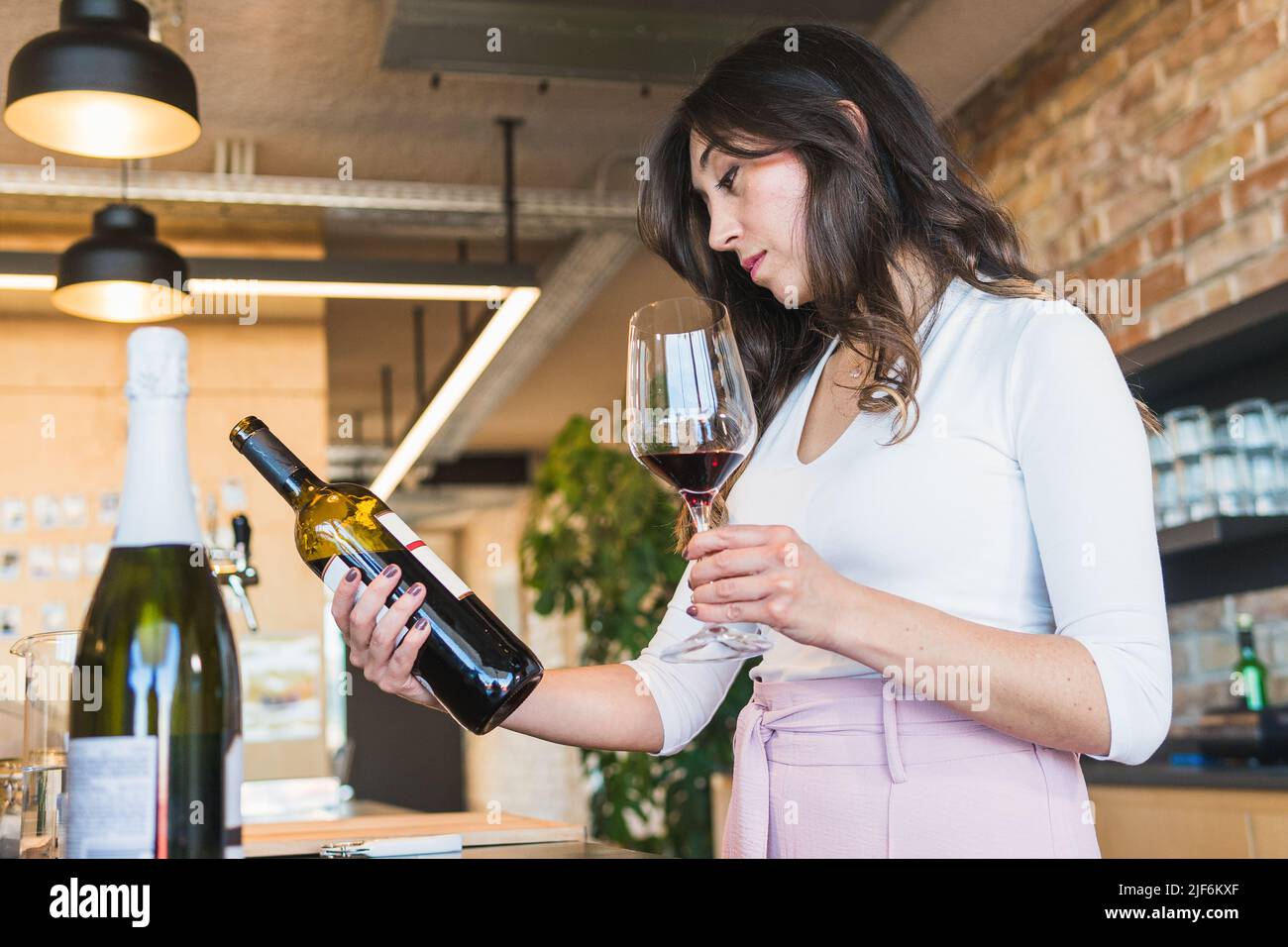 Side view of young brunette with red wine in glass goblet holding ...