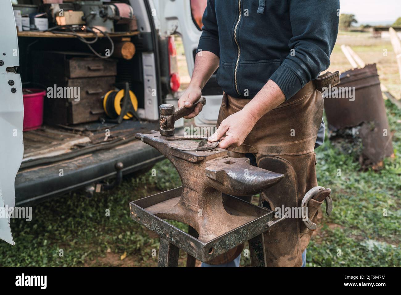 Crop faceless worker in uniform forging horseshoe with hammer on metal ...