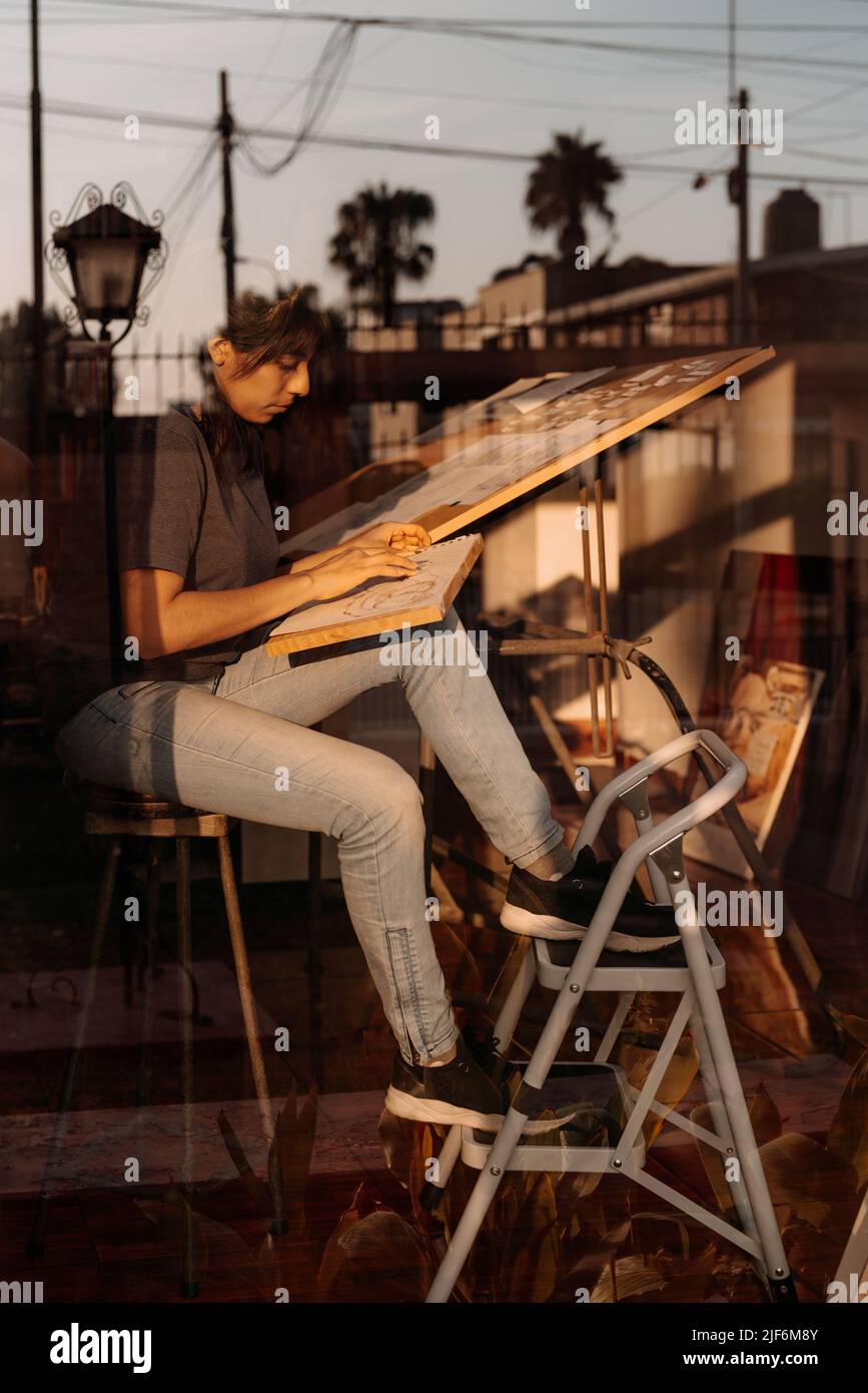 Side view through the glass of a Woman drawing at home at sunset Stock ...