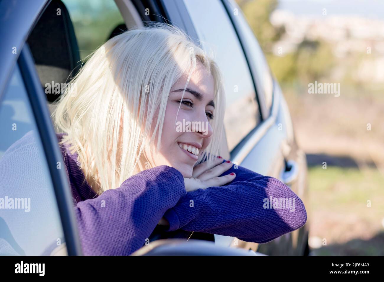 Smiling young woman looks out of a car window Stock Photo - Alamy