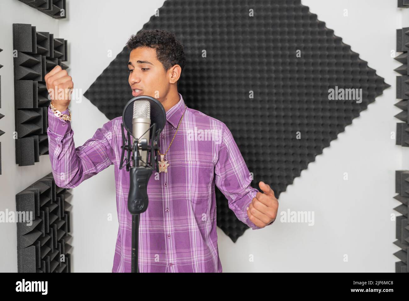 Young man singing in microphone while recording voice in music studio ...