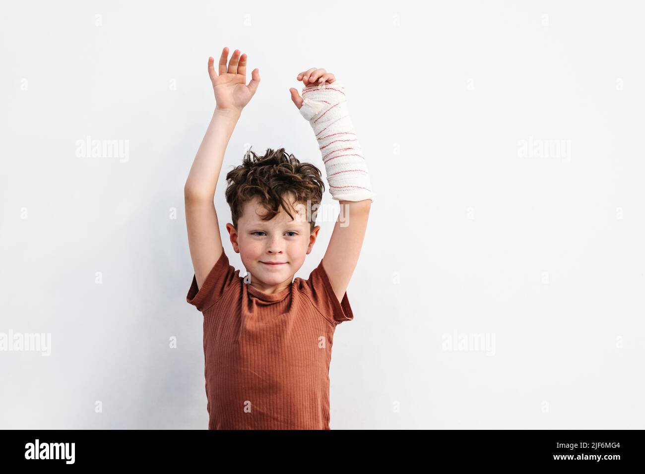 Adorable playful boy in brown t shirt and raising arms with broken arm ...