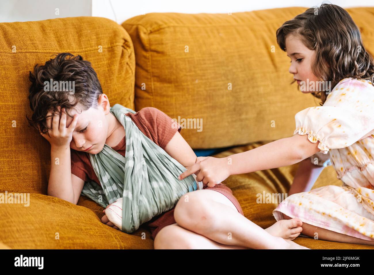 Adorable girl in dress poking bandaged arm of boy touching forehead and ...