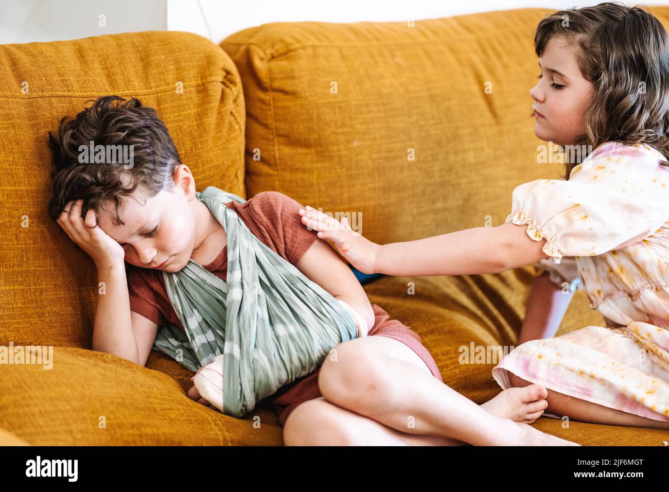 Adorable girl in dress poking bandaged arm of boy touching forehead and ...