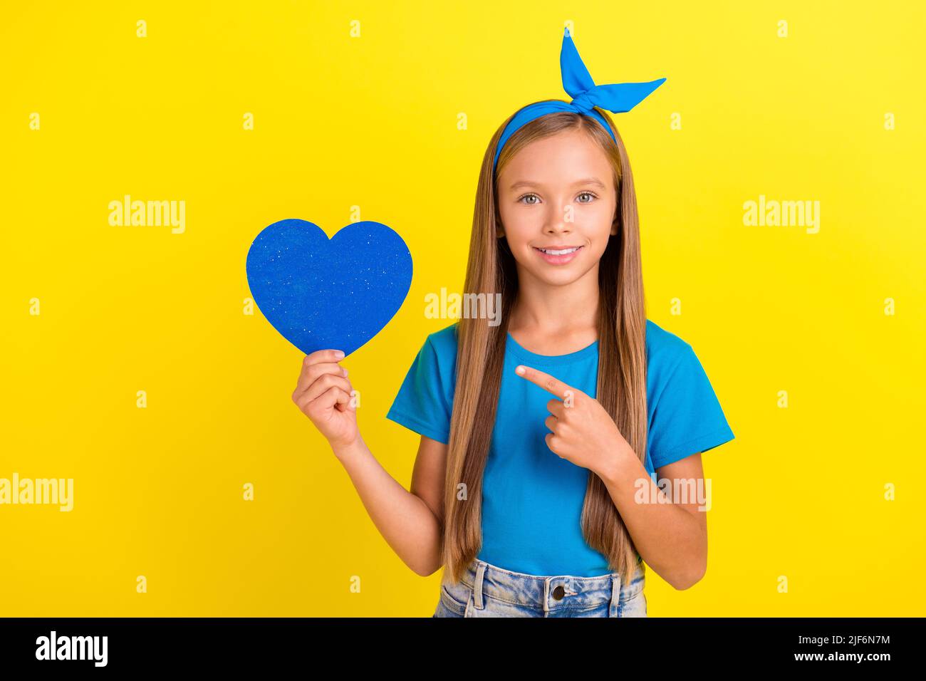 Photo of small cheerful schoolgirl direct finger hand hold paper heart ...