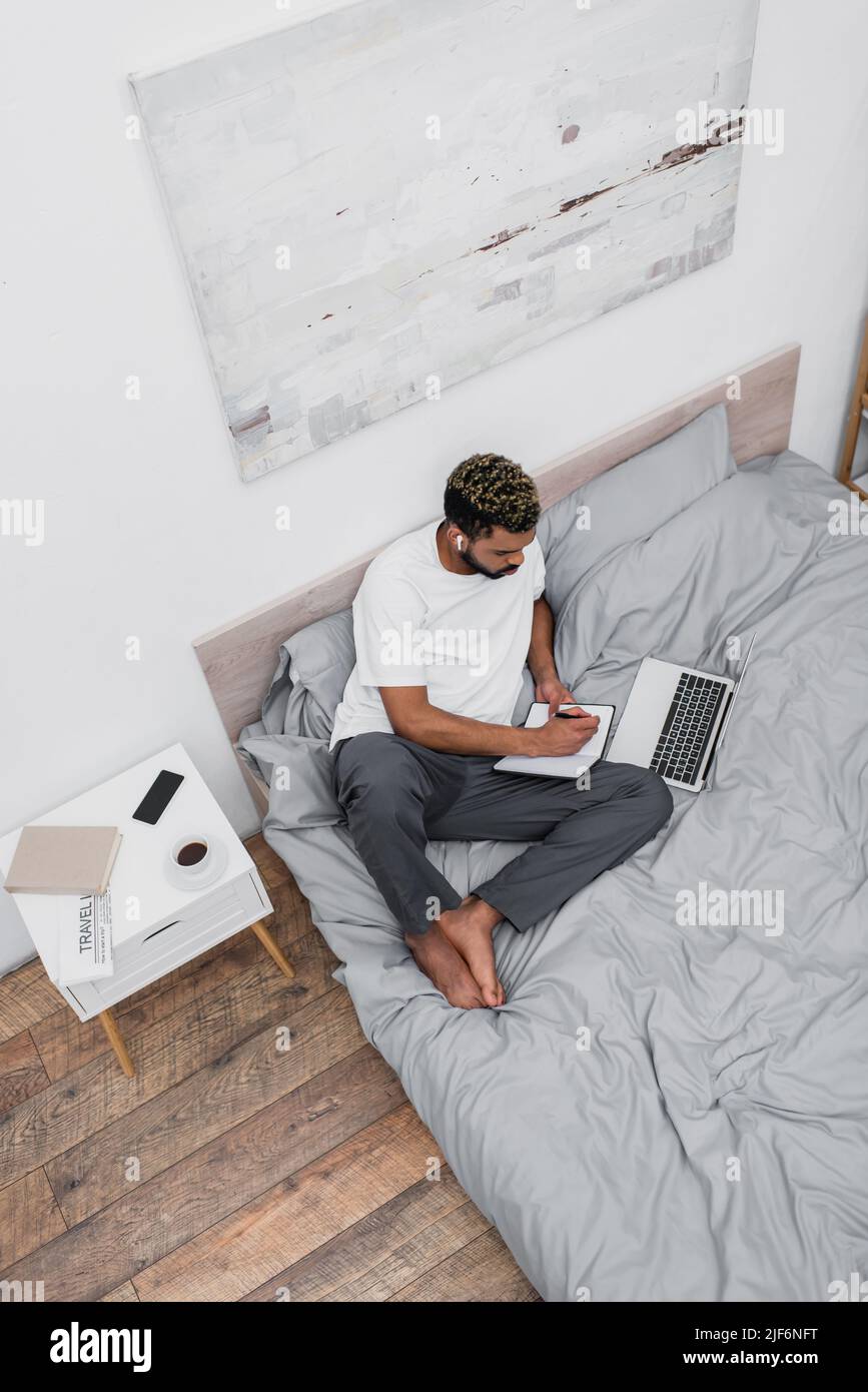 top view of african american man in wireless earphones using laptop and ...