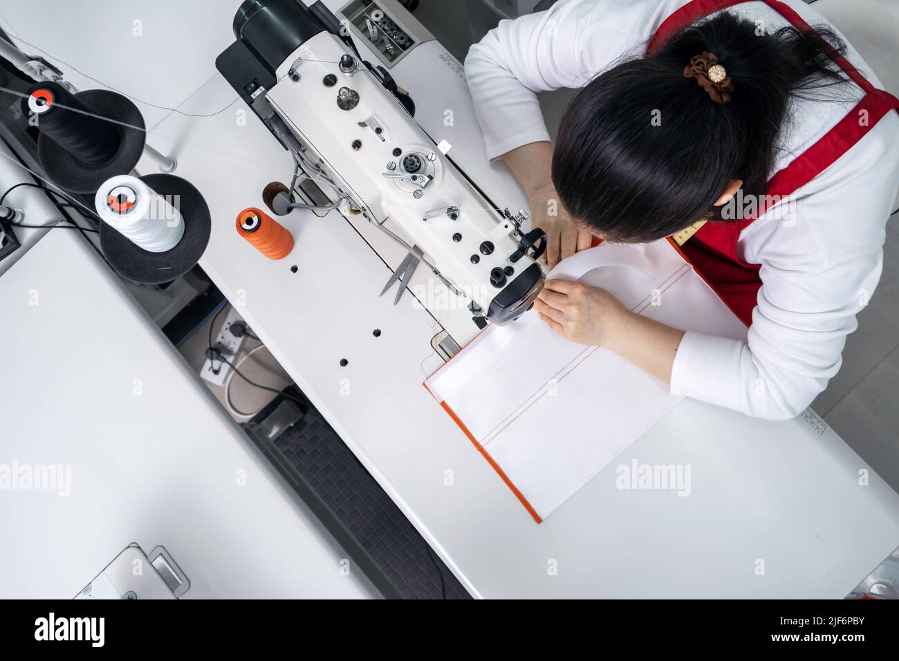 From above of anonymous dressmaker in uniform sewing on machine while ...