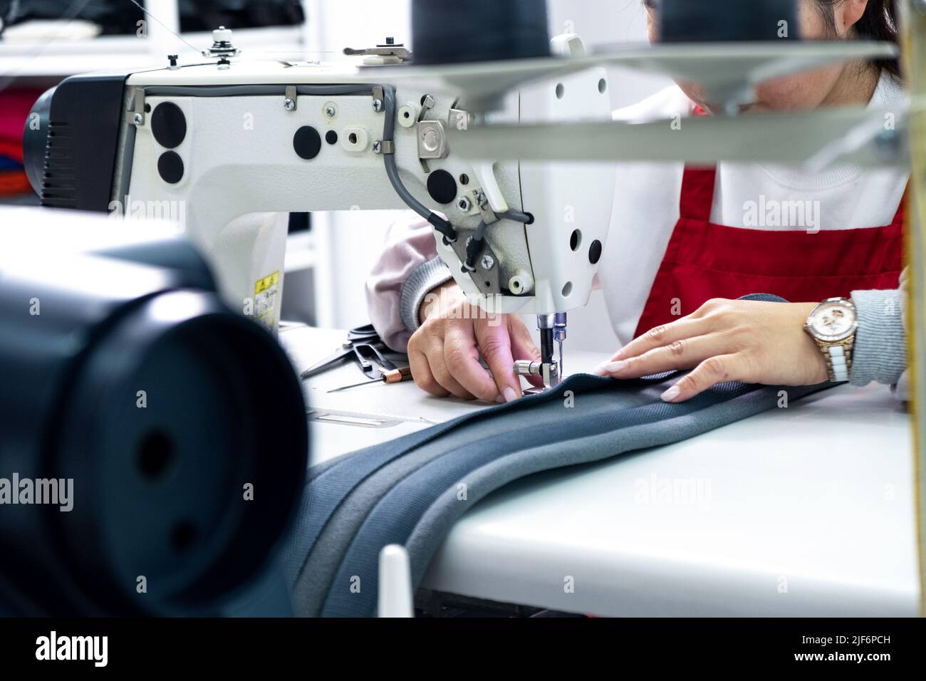 Anonymous cropped dressmaker in uniform sewing on machine while working ...