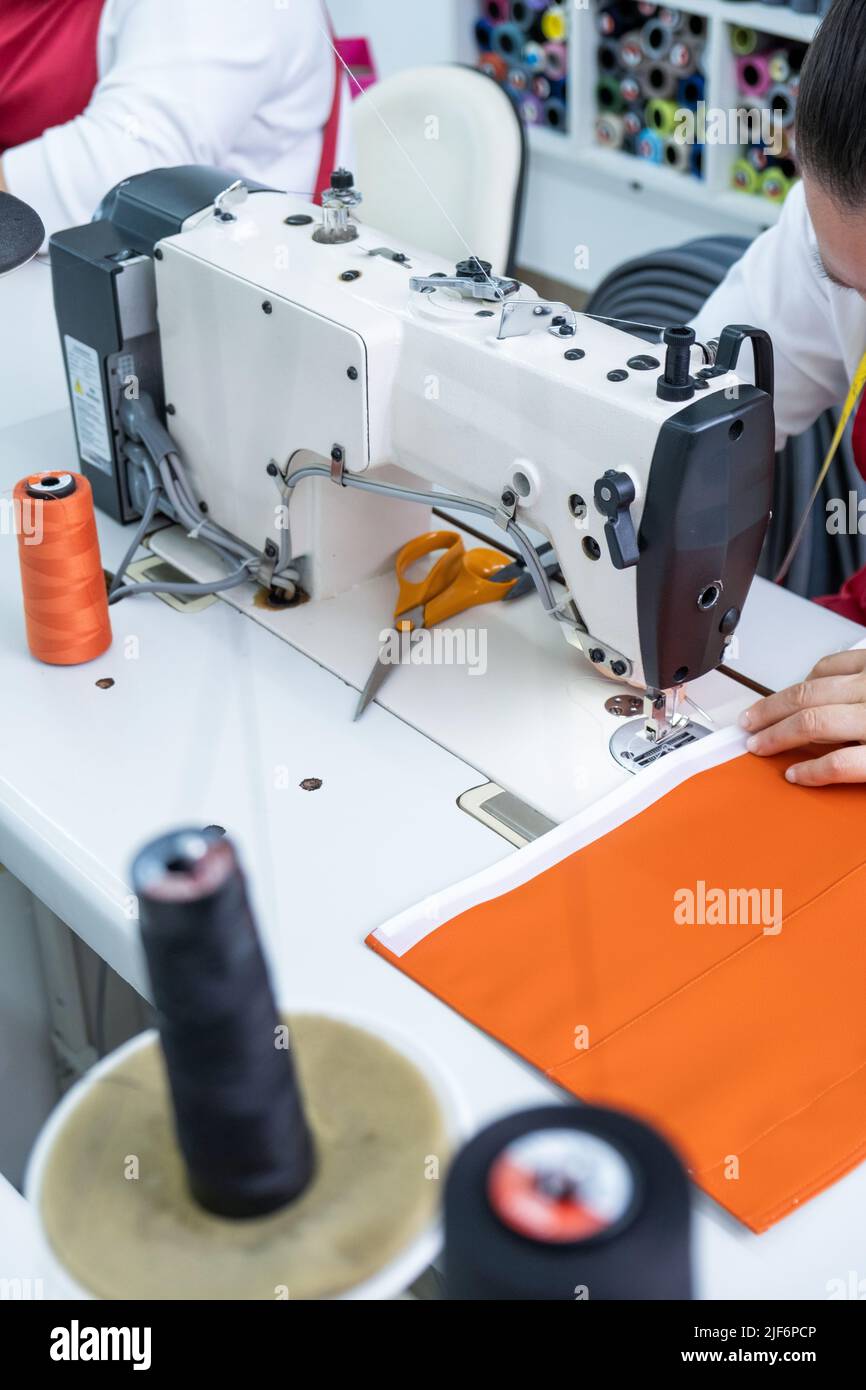 Anonymous cropped dressmaker in uniform sewing on machine while working ...