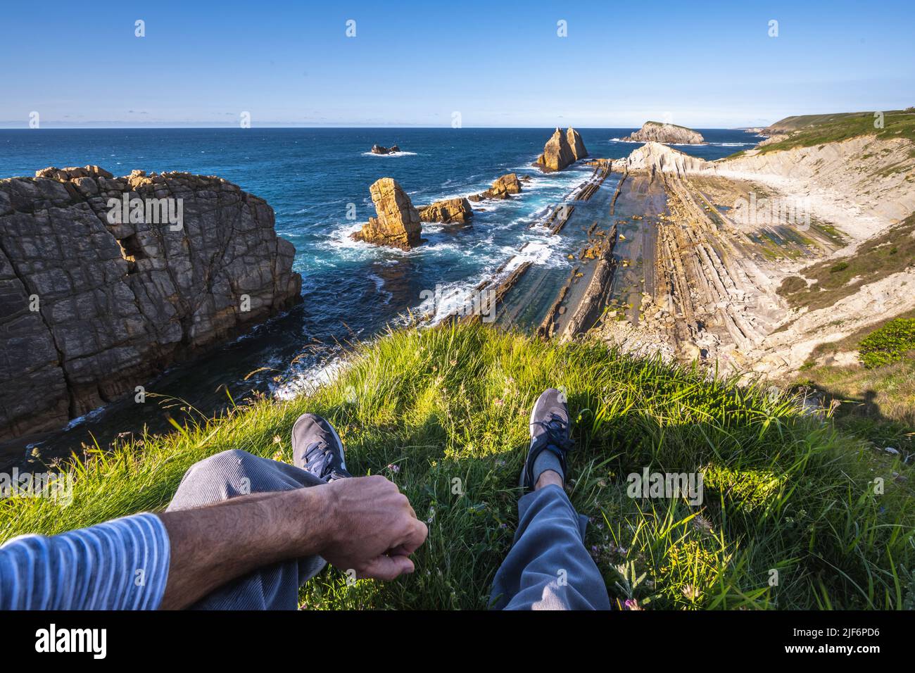 Low section of male hiker sitting on cliff enjoying the view of sea ...