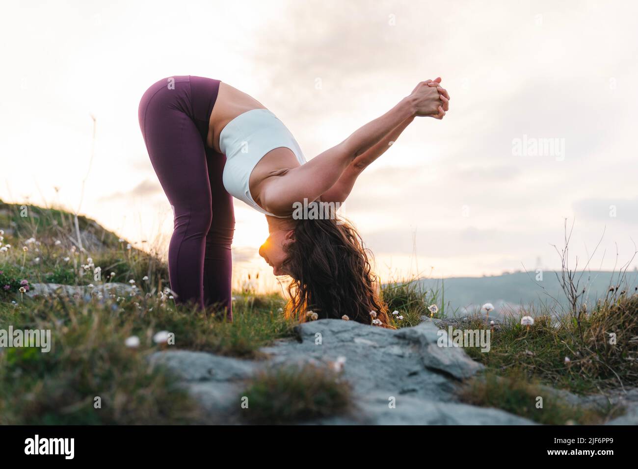 Side view of flexible young lady with long wavy hair in activewear ...