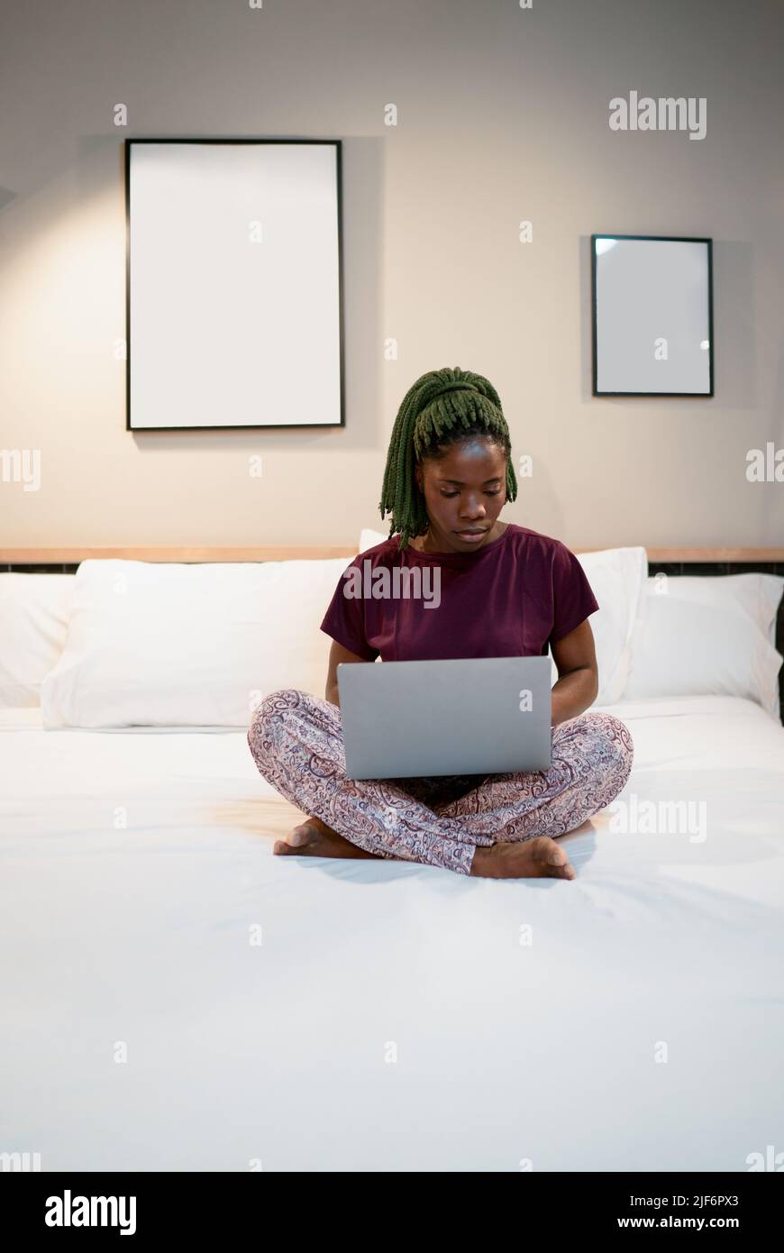 Full body of young ethnic female sitting on bed and browsing netbook ...