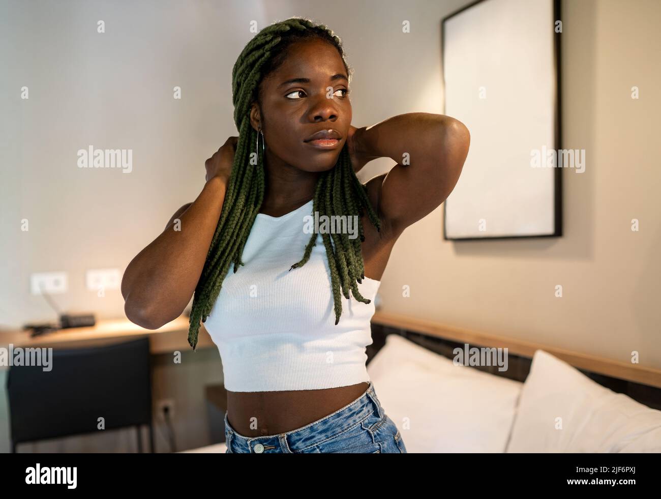 Thoughtful ethnic female touching long braided hair and looking away in ...