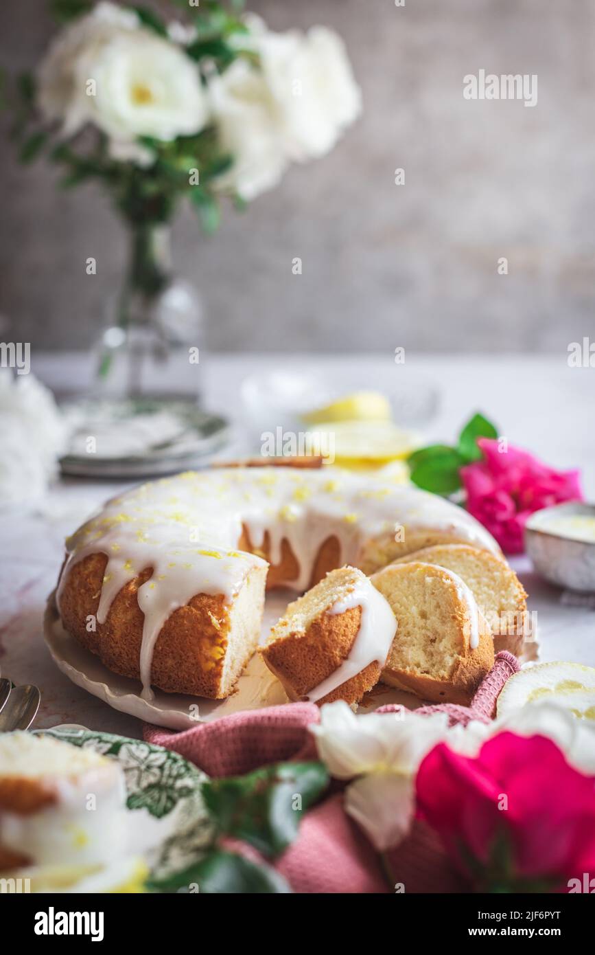 Sponge lemon cake on a table next to white and pink roses with petals ...
