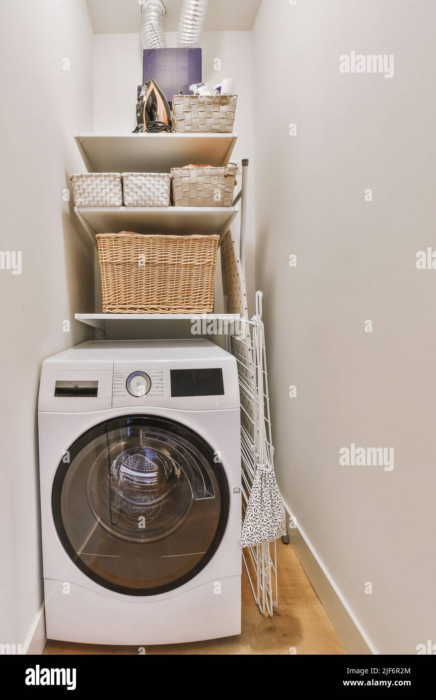 Modern white electric washing machine under shelf near various utensils ...