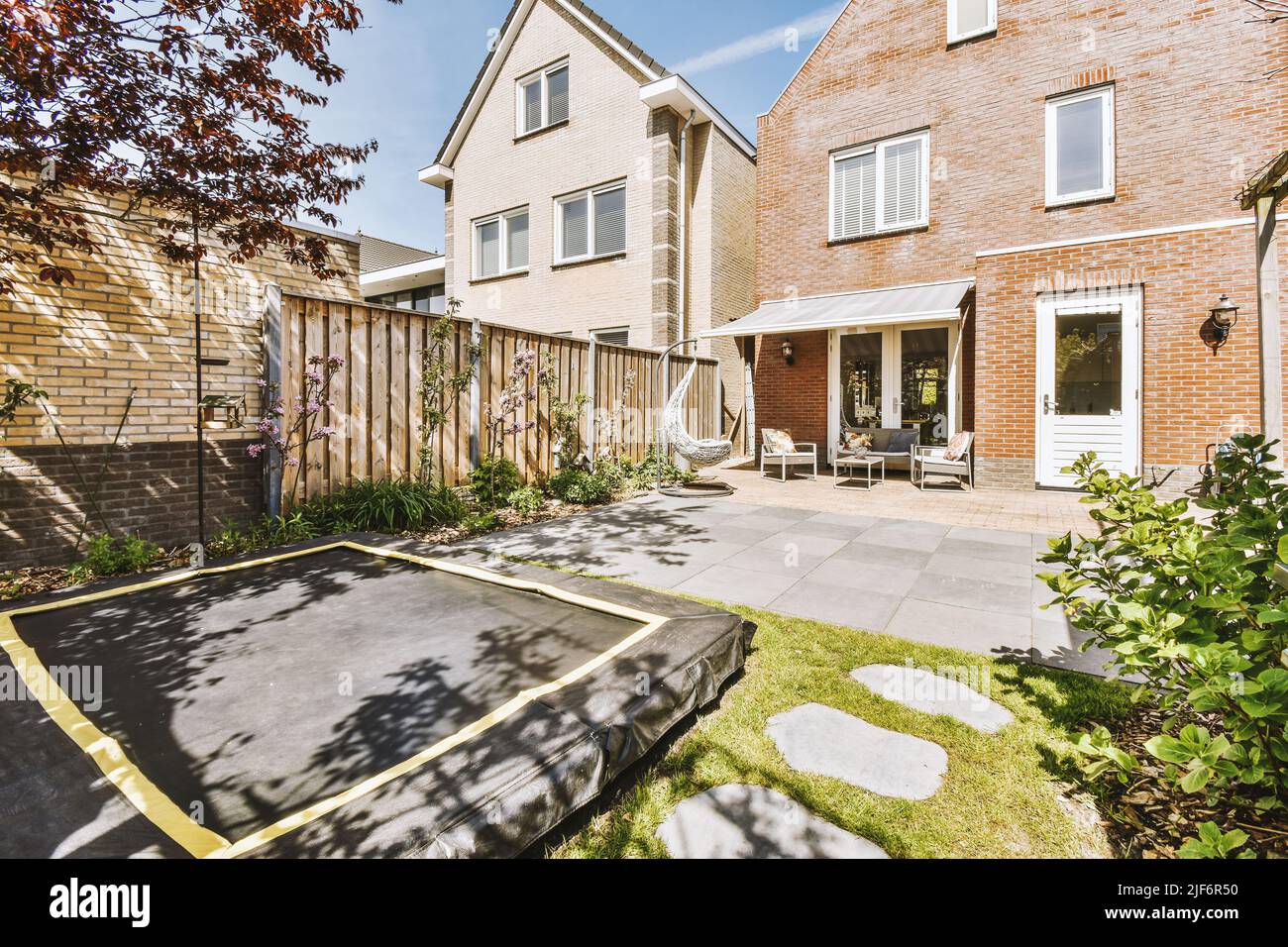 Neat paved patio with sitting area and small garden near wooden fence ...