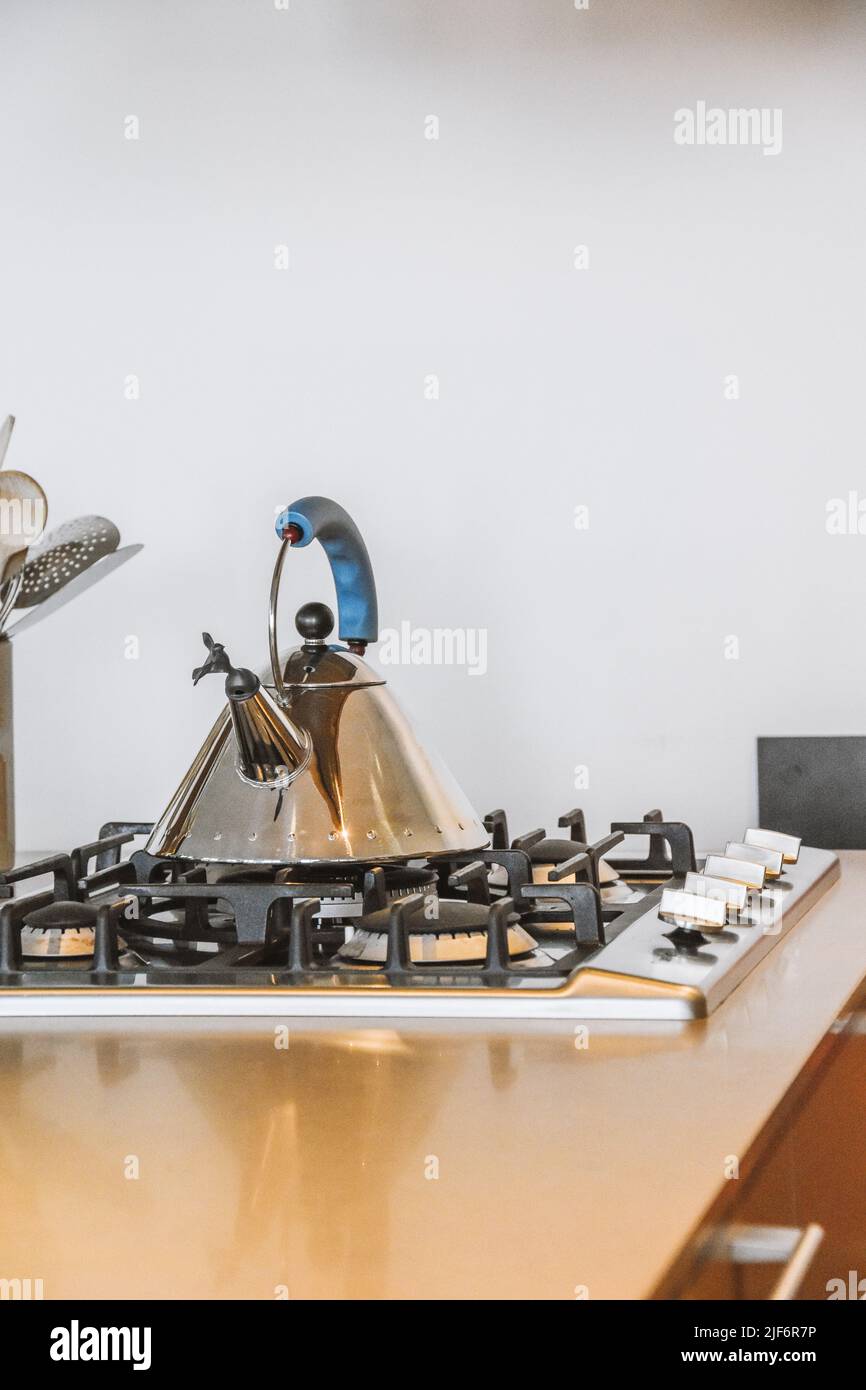 Shiny kettle placed on built in gas cooker against gray wall in modern ...
