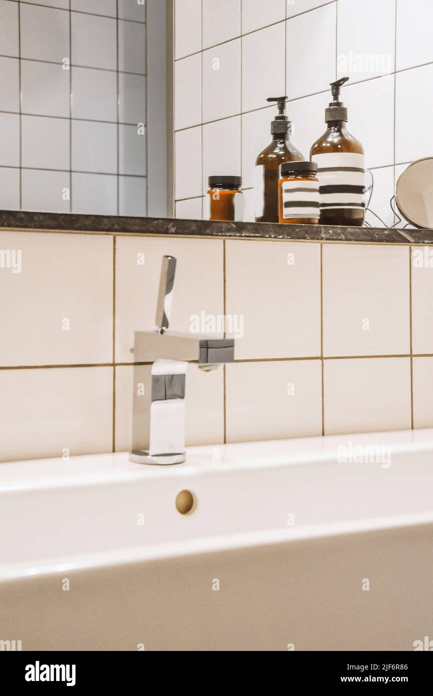 sink taps installed on tiled walls near bottles with cosmetic products ...