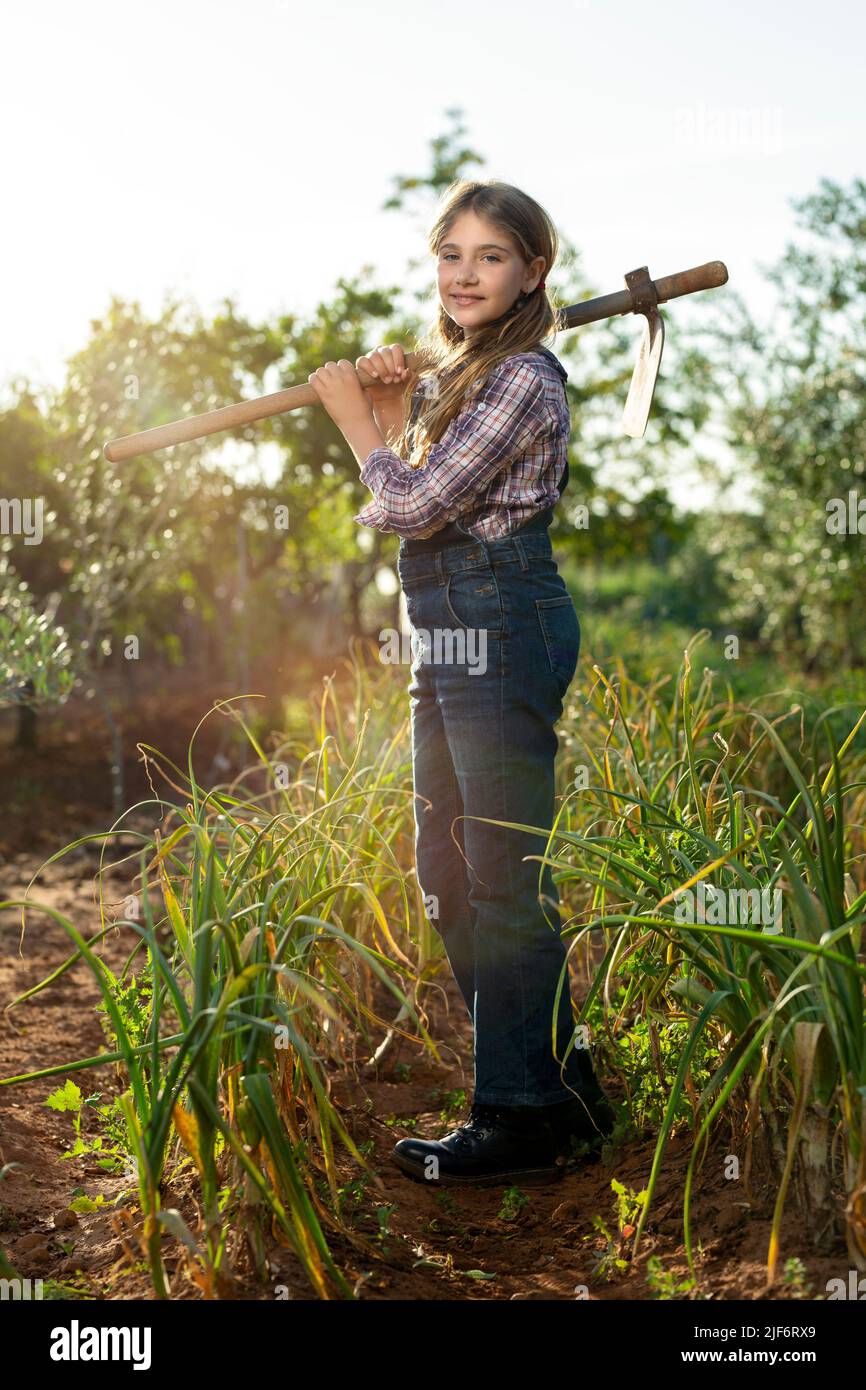 Full body confident girl in checkered shirt and jeans carrying hoe on ...