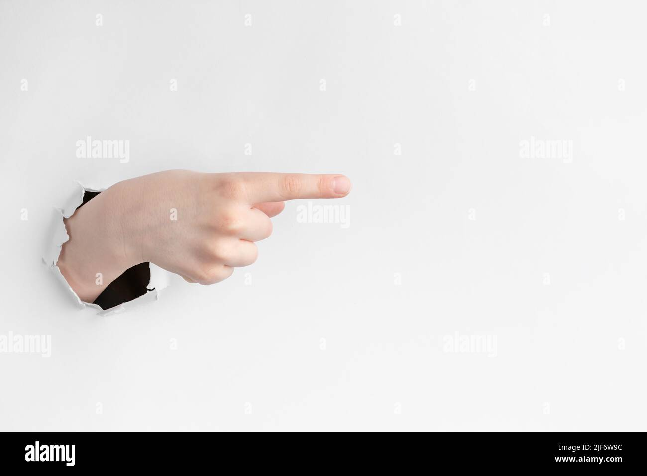 child hand pointing the forefinger to the right through hole in white ...