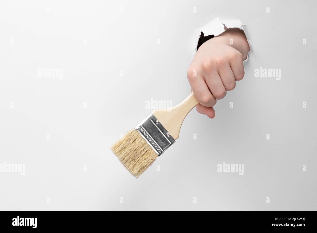 child hand through hole in white paper with torn edges holding a paint ...