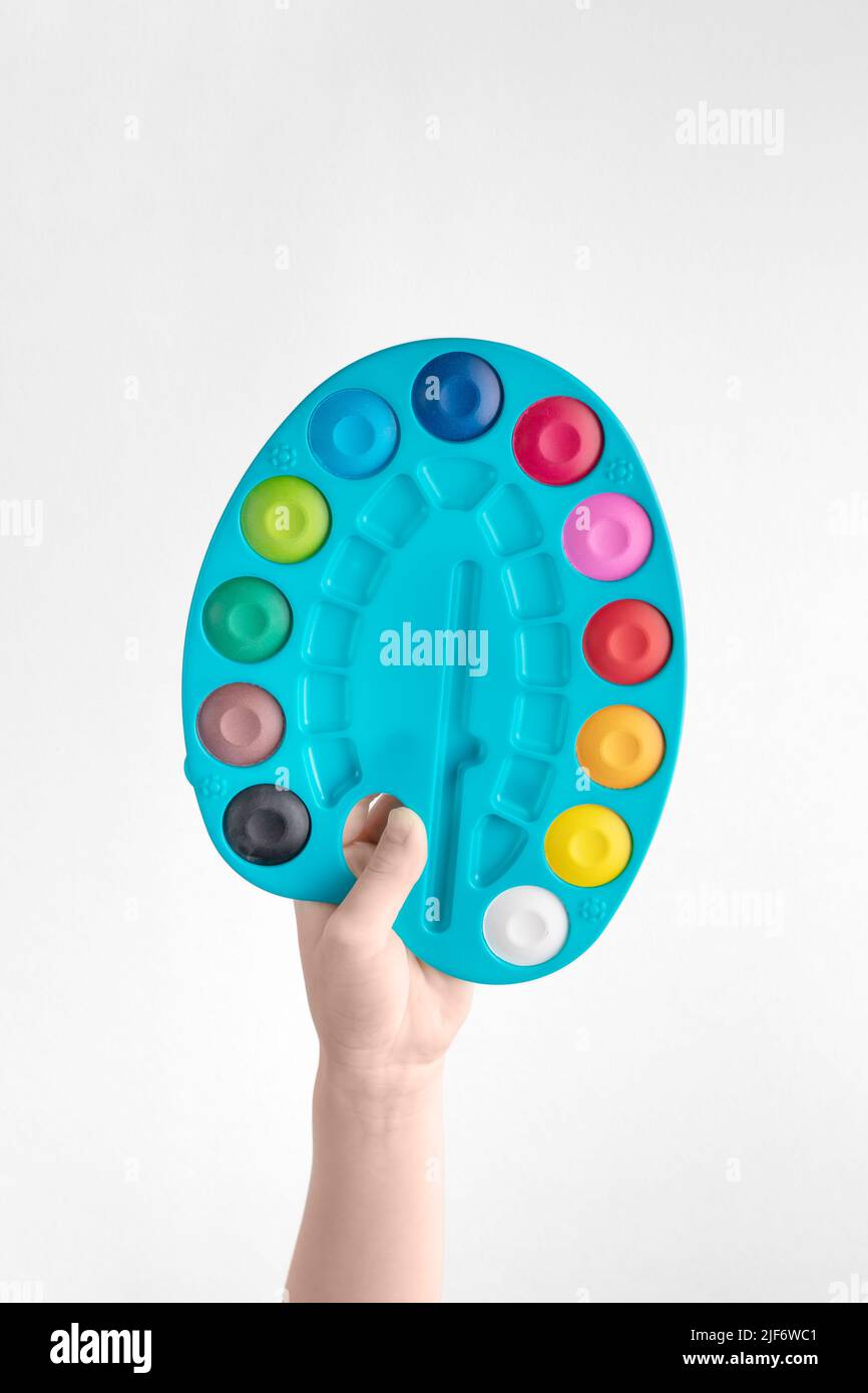 child hand holding a paint palette above a white and gray paper ...