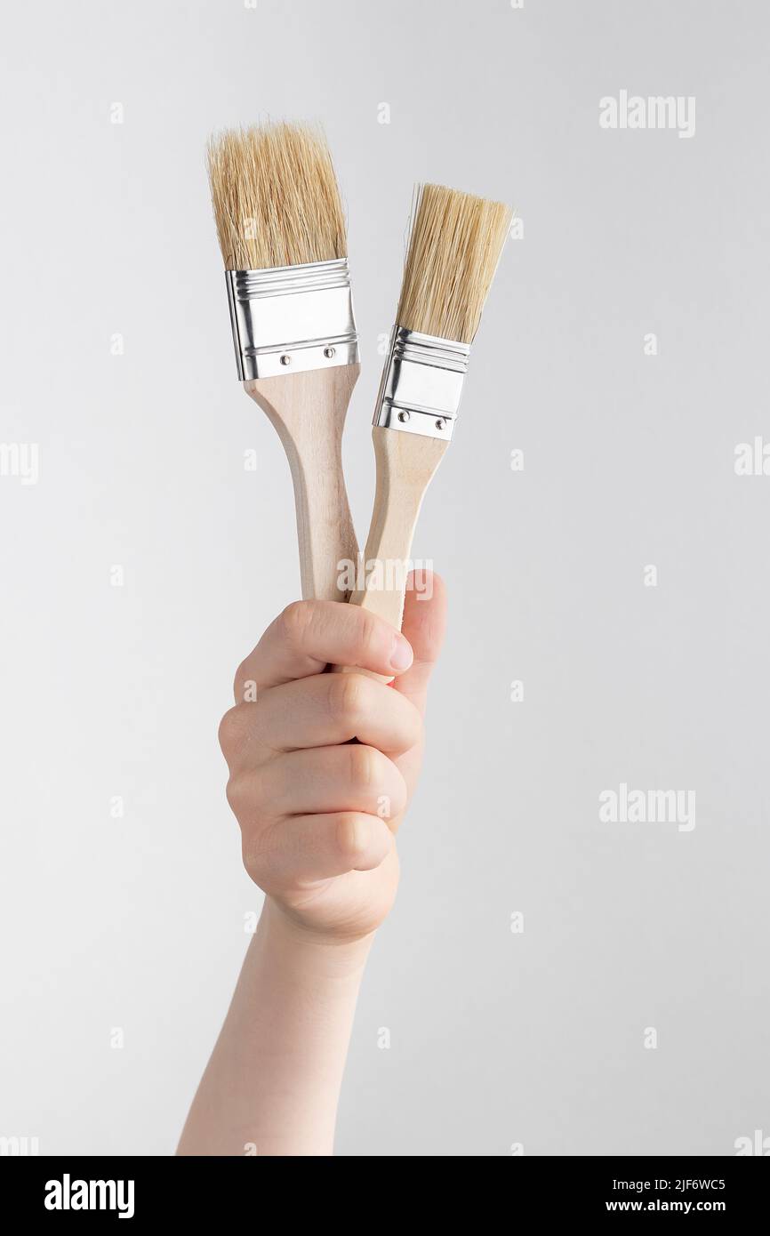 child hand holding two paint brushes above a white and gray paper ...