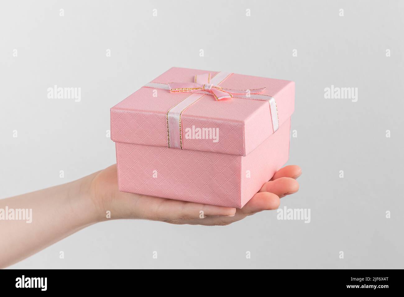 Child hand holding gift box with pink bow. white and gray background ...