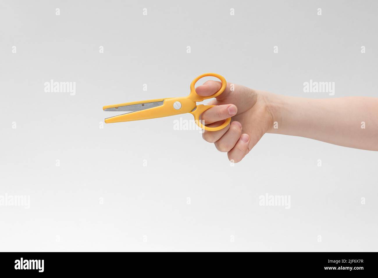 Child hand holding yellow scissors for left-handers. white and gray ...
