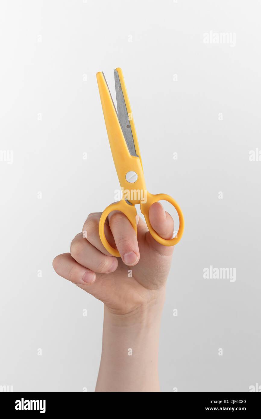 Child hand holding yellow scissors for left-handers. white and gray ...