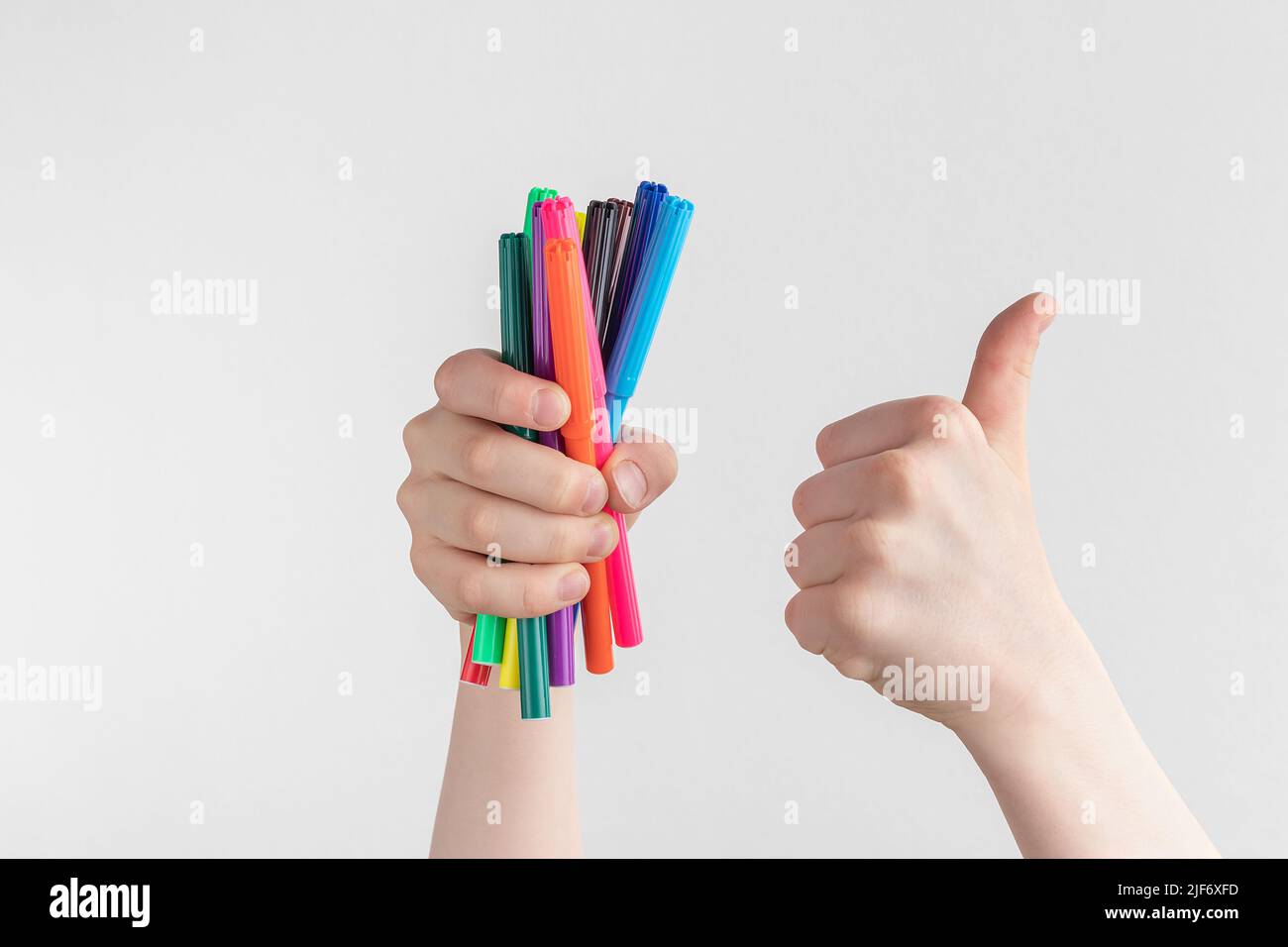 child hand holding many colorful felt-tip pens and showing thumbs up ...