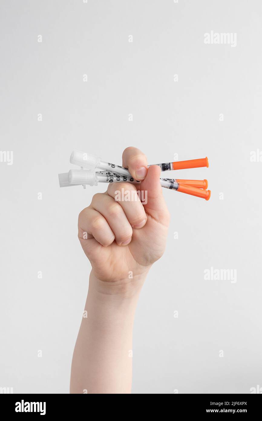 child hand holding a insulin syringe. white and gray background with ...