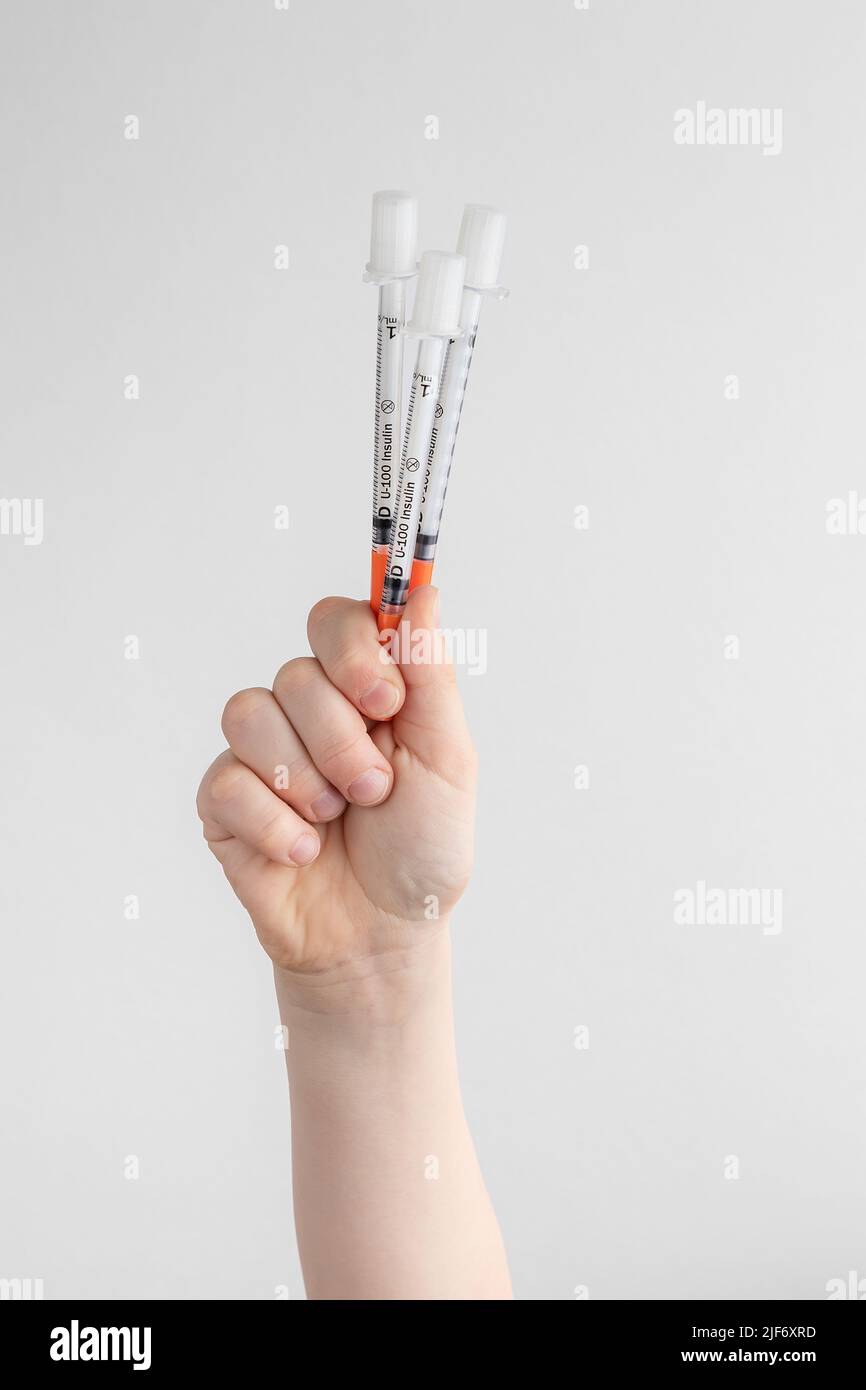 child hand holding a insulin syringe. white and gray background with ...