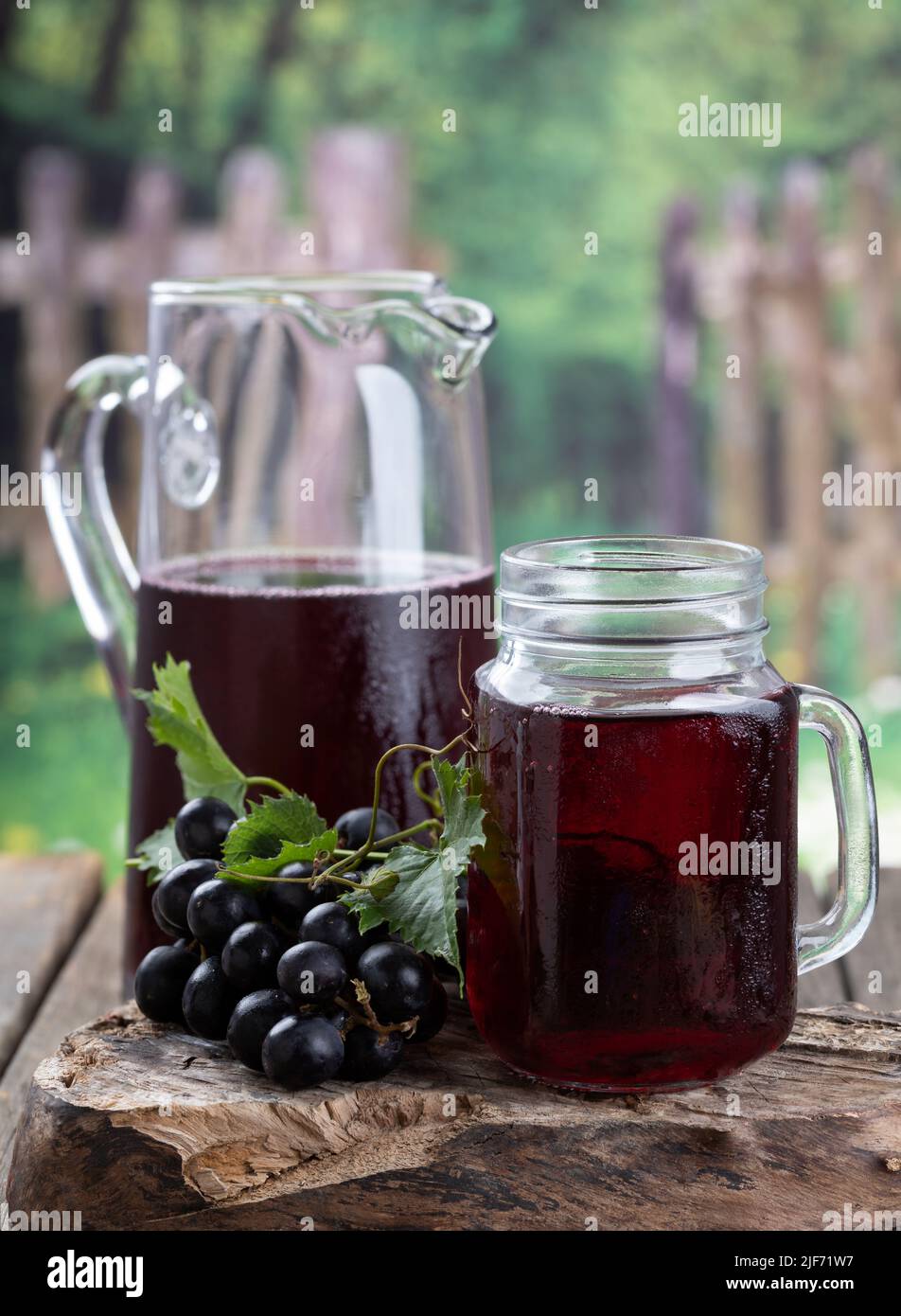 Glass and pitcher of grape juice with fresh grapes on wooden block with ...