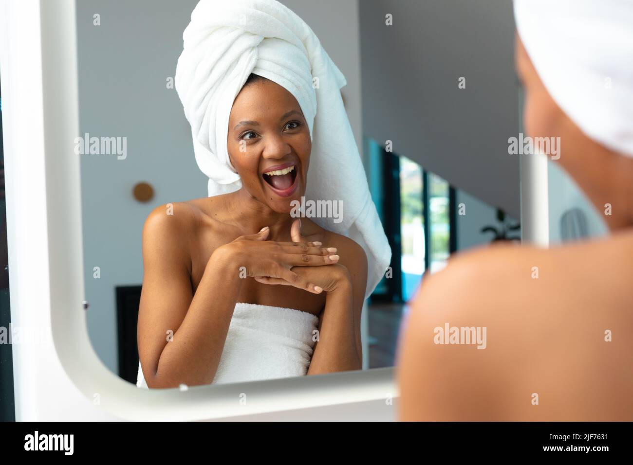 Happy excited young african american woman looking herself in mirror at ...