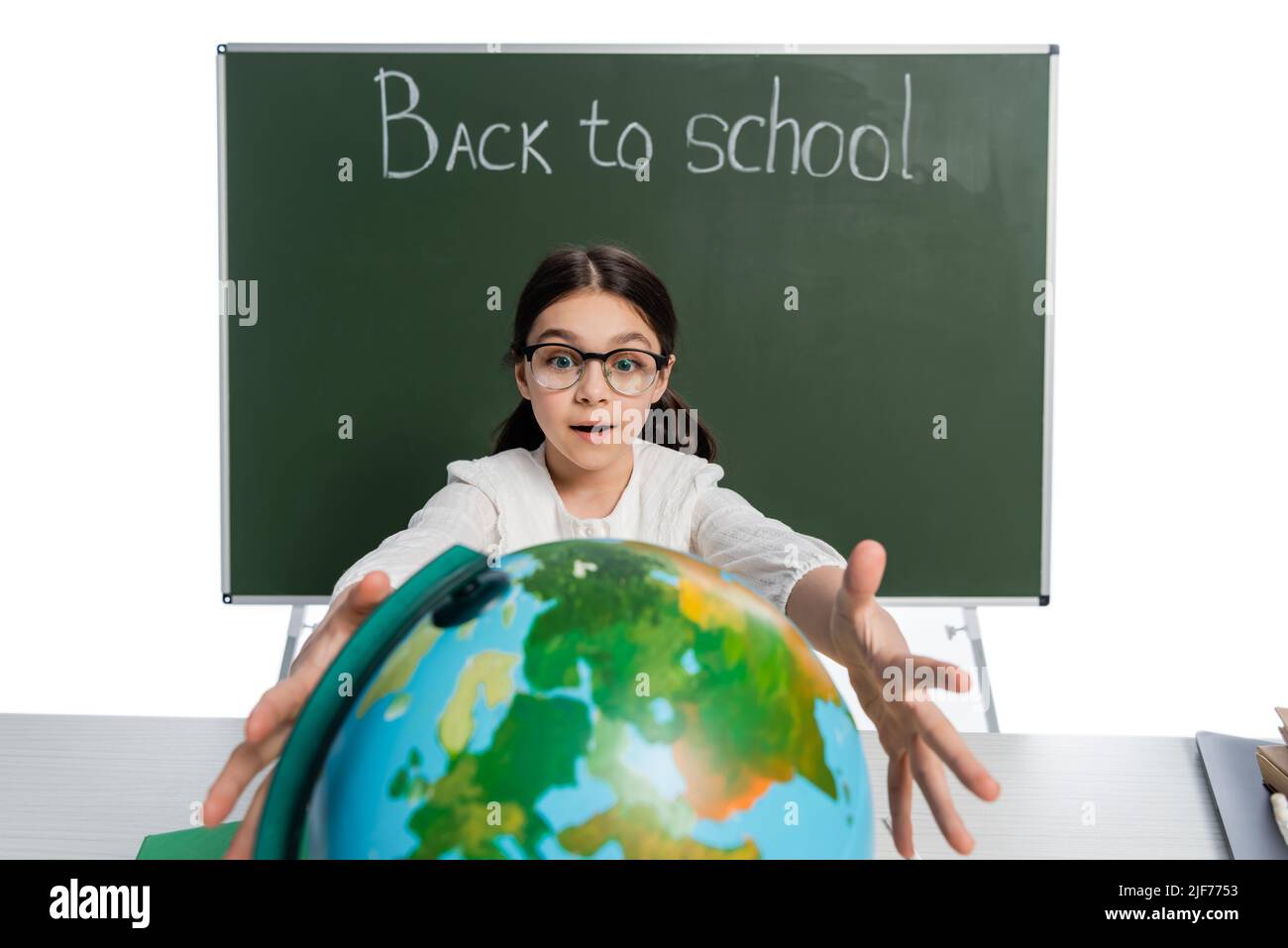 Excited schoolgirl outstretching hands to globe near chalkboard with ...