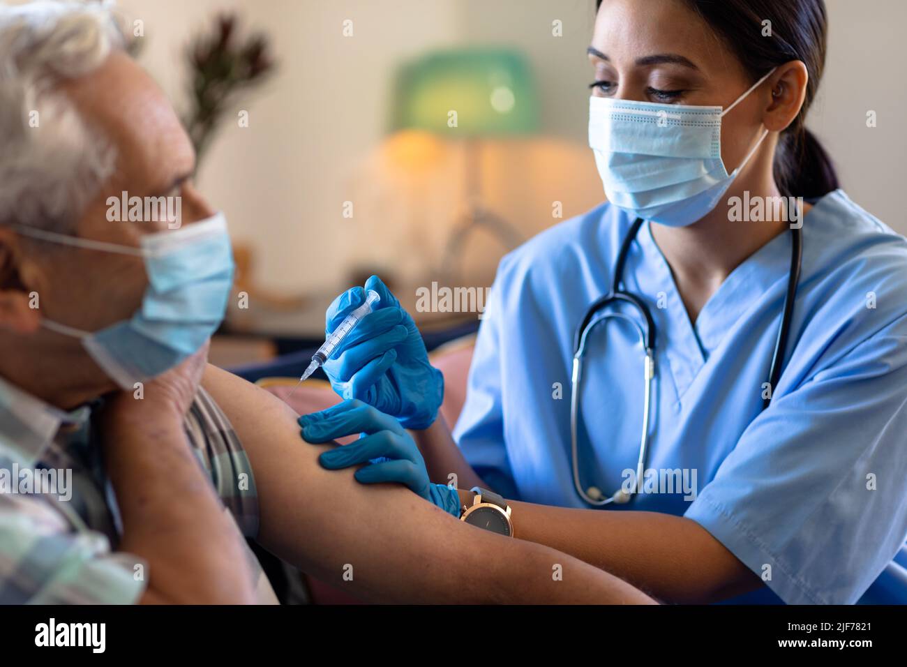 Biracial female health worker giving an injection to caucasian senior ...