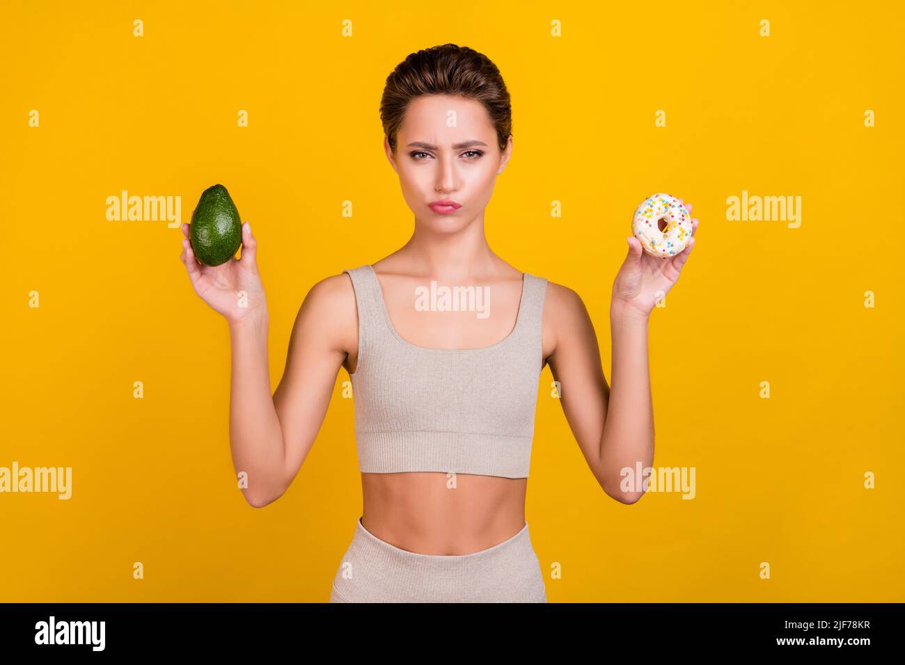 Photo of thoughtful minded lady hold avocado doughnut choose wear grey ...