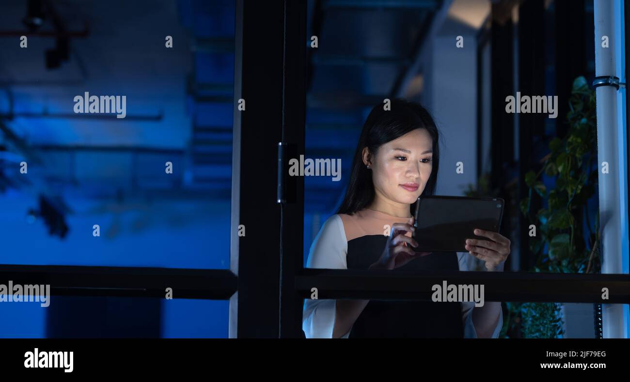 Asian businesswoman using digital tablet while standing by window in ...